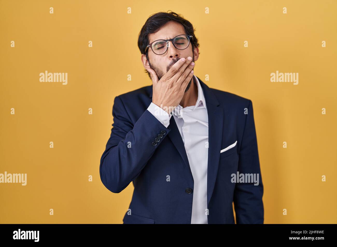 Handsome latin man standing over yellow background bored yawning tired ...