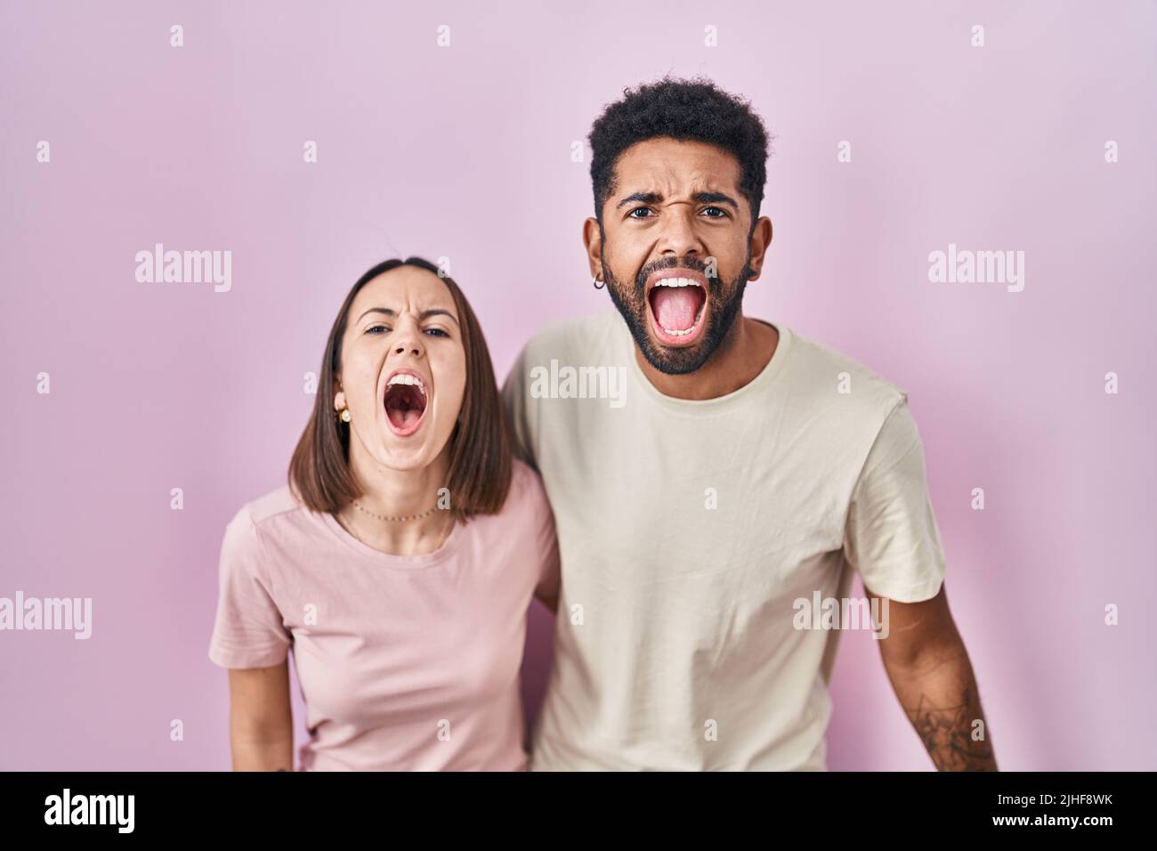 Young hispanic couple together over pink background angry and mad ...