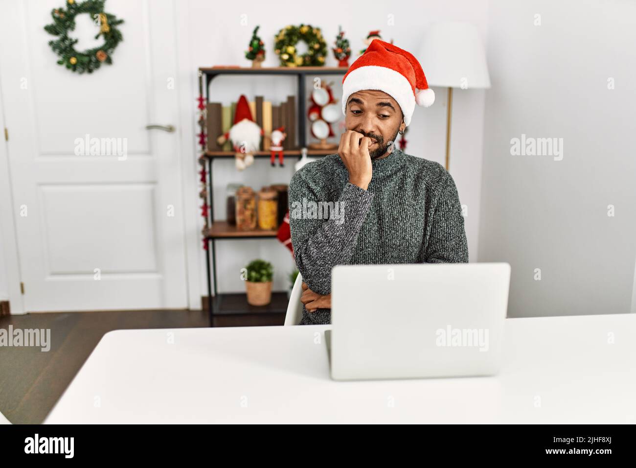Young hispanic man with beard wearing christmas hat using laptop ...