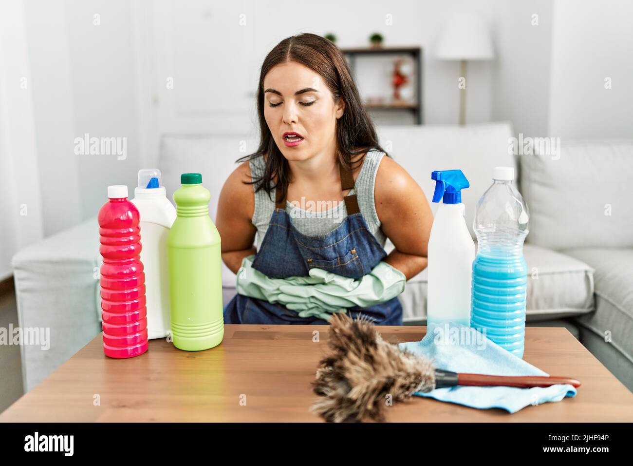 Young brunette woman wearing cleaner apron and gloves cleaning at home ...
