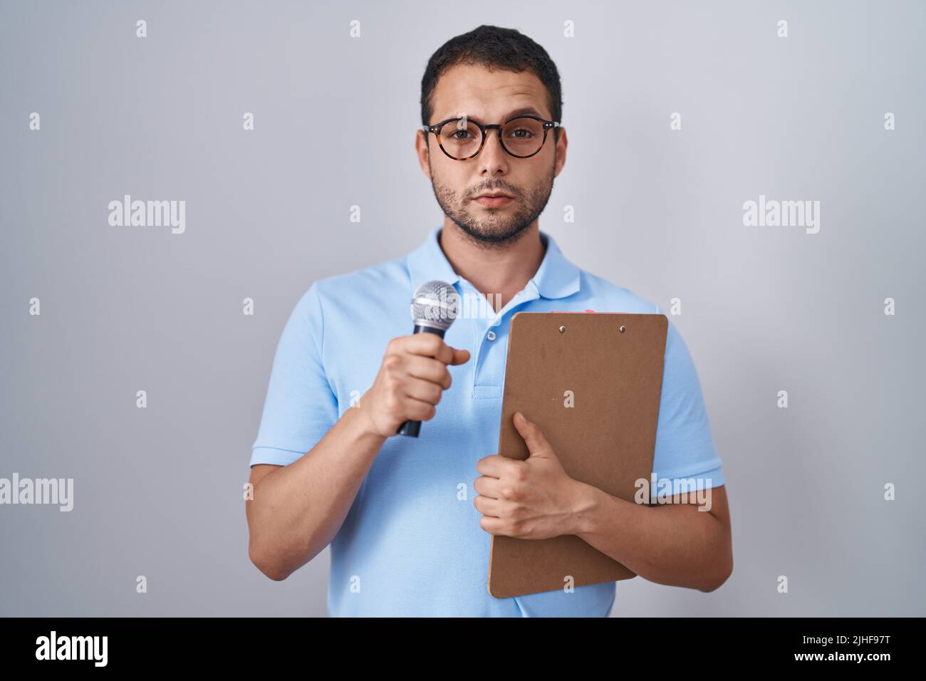 Hispanic man holding reporter microphone and clipboard depressed and ...