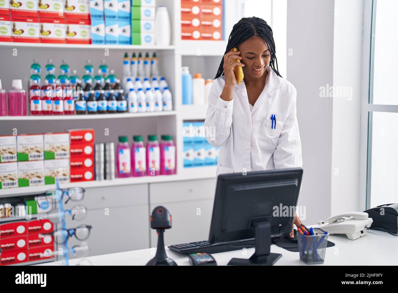 African american woman pharmacist talking on smartphone using computer ...