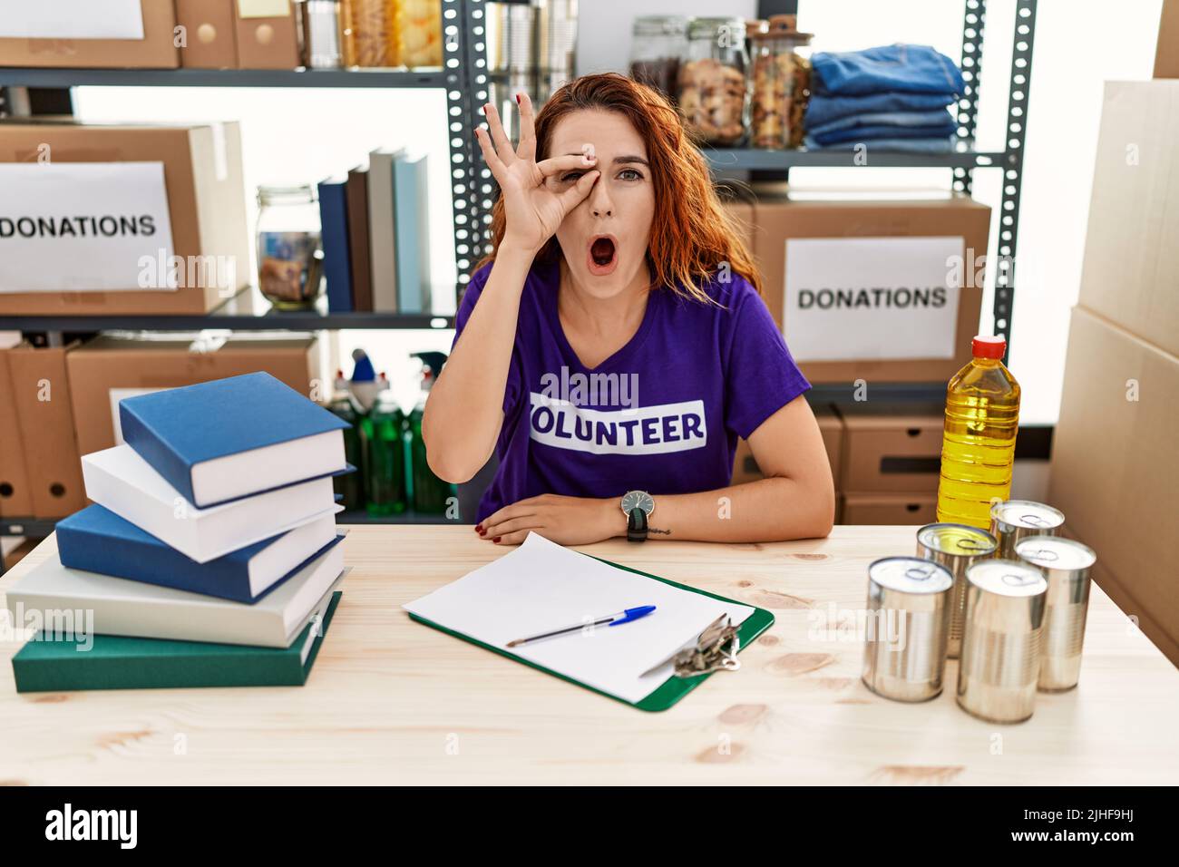 Young redhead woman wearing volunteer t shirt at donations stand doing ...
