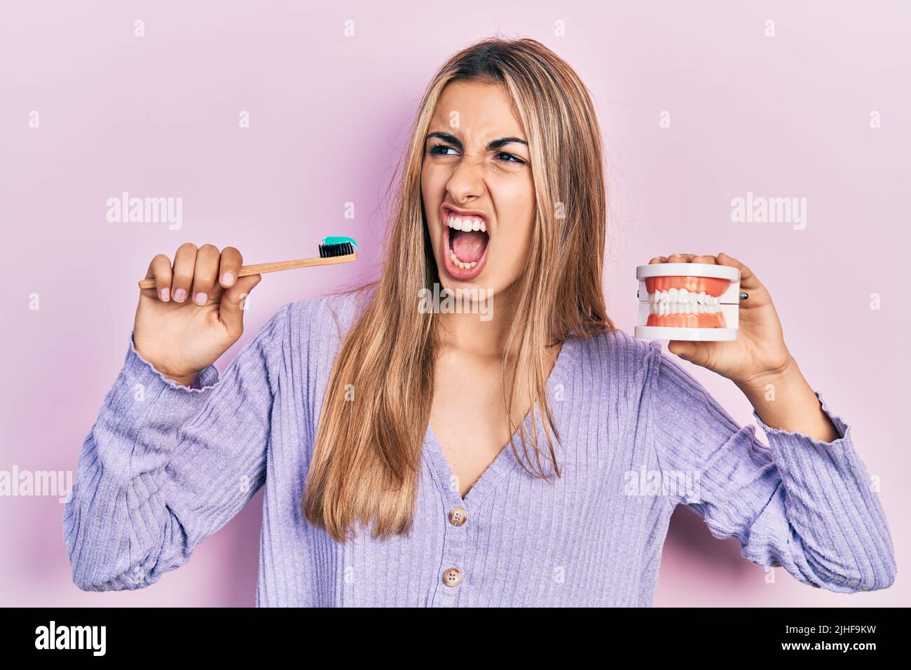 Beautiful hispanic woman holding denture and toothbrush angry and mad ...