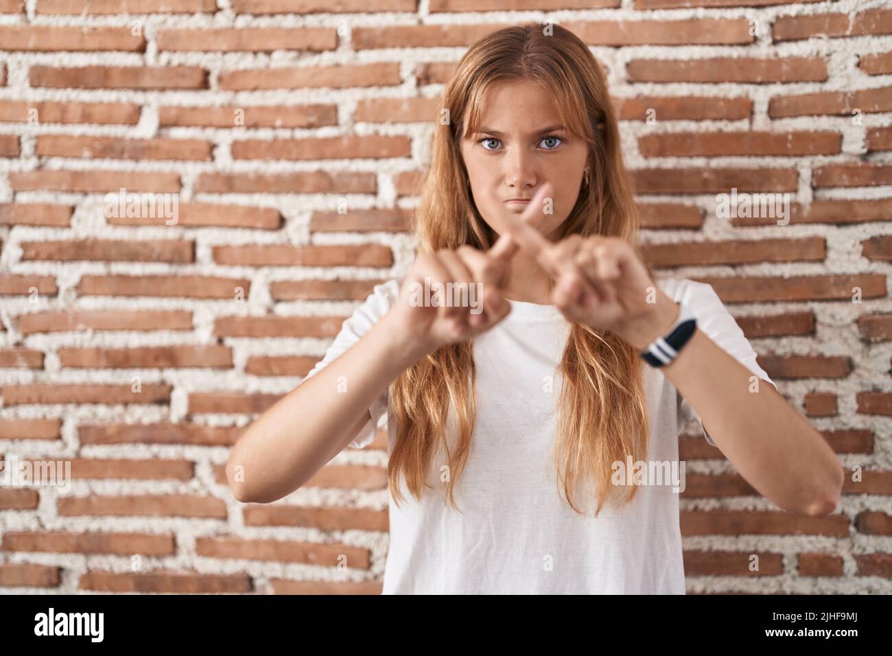 Young caucasian woman standing over bricks wall rejection expression ...