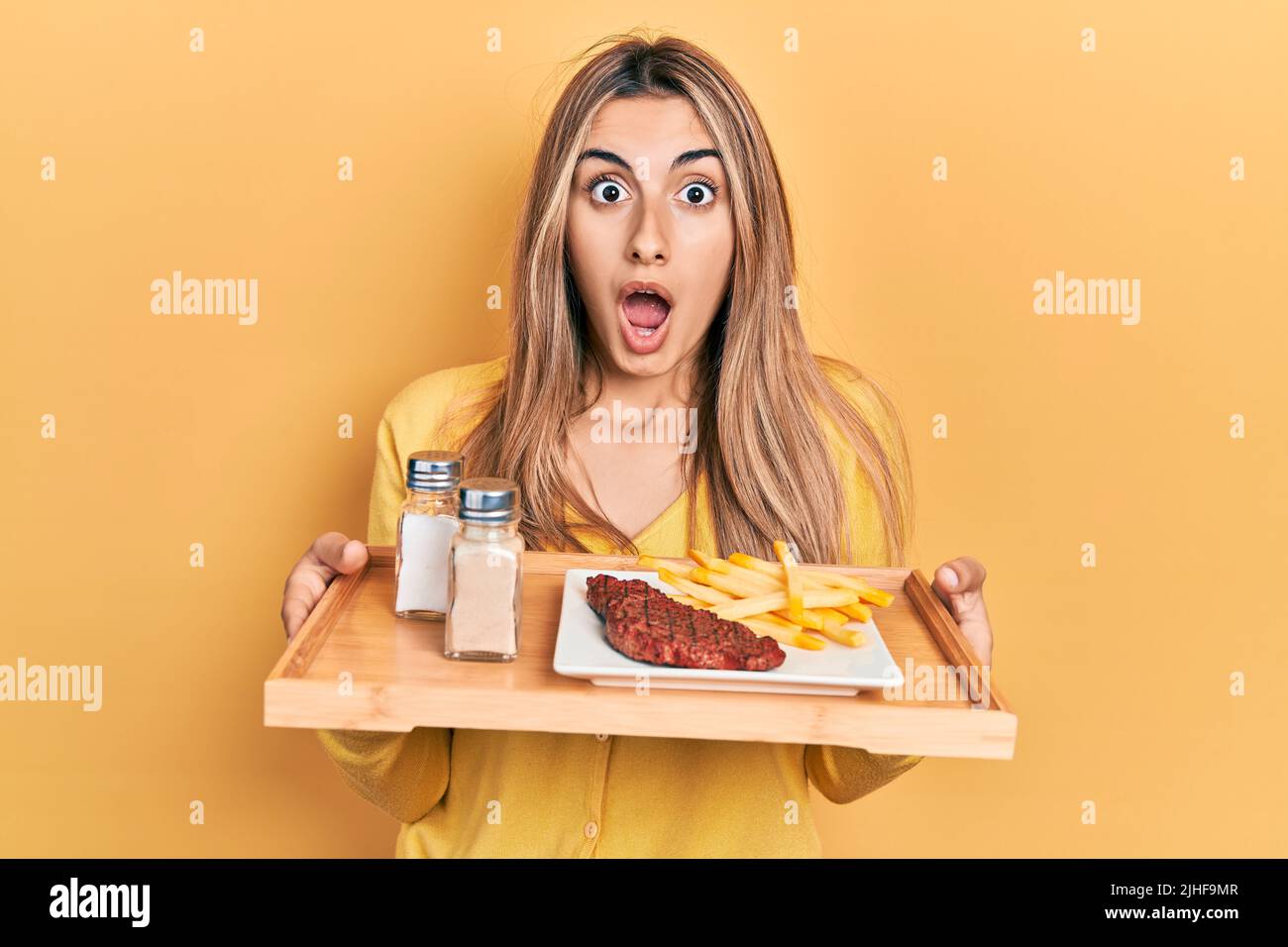 Beautiful hispanic woman holding tray with lunch afraid and shocked ...