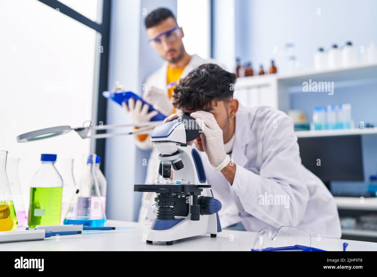 Two man scientists using microscope write on clipboard working at ...