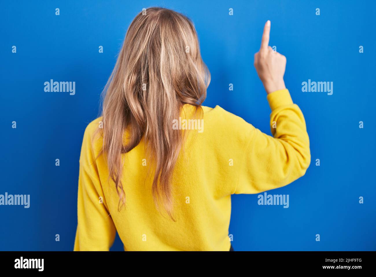 Young caucasian woman standing over blue background posing backwards ...