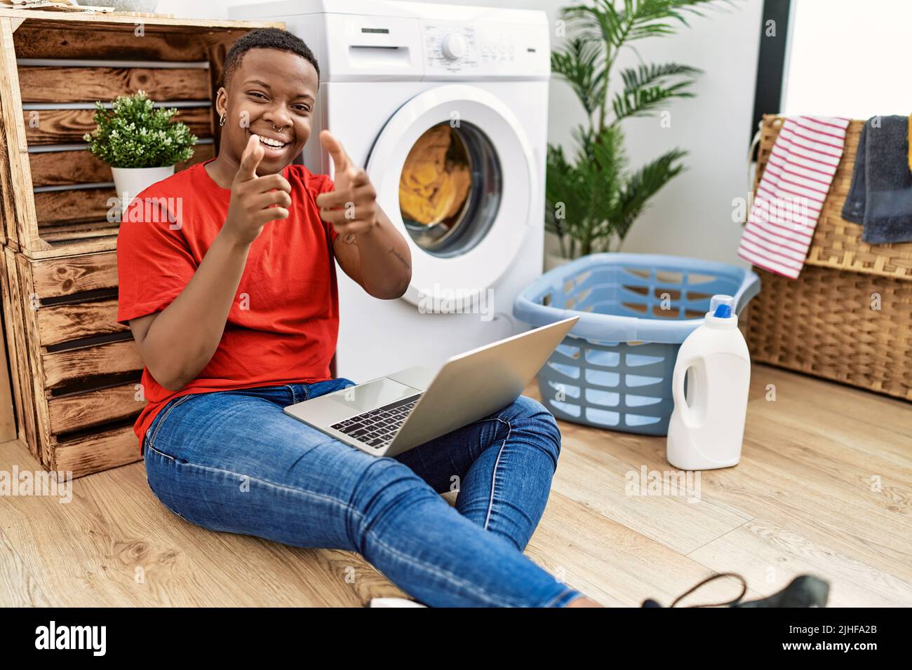 Young african man doing laundry and using computer pointing fingers to ...