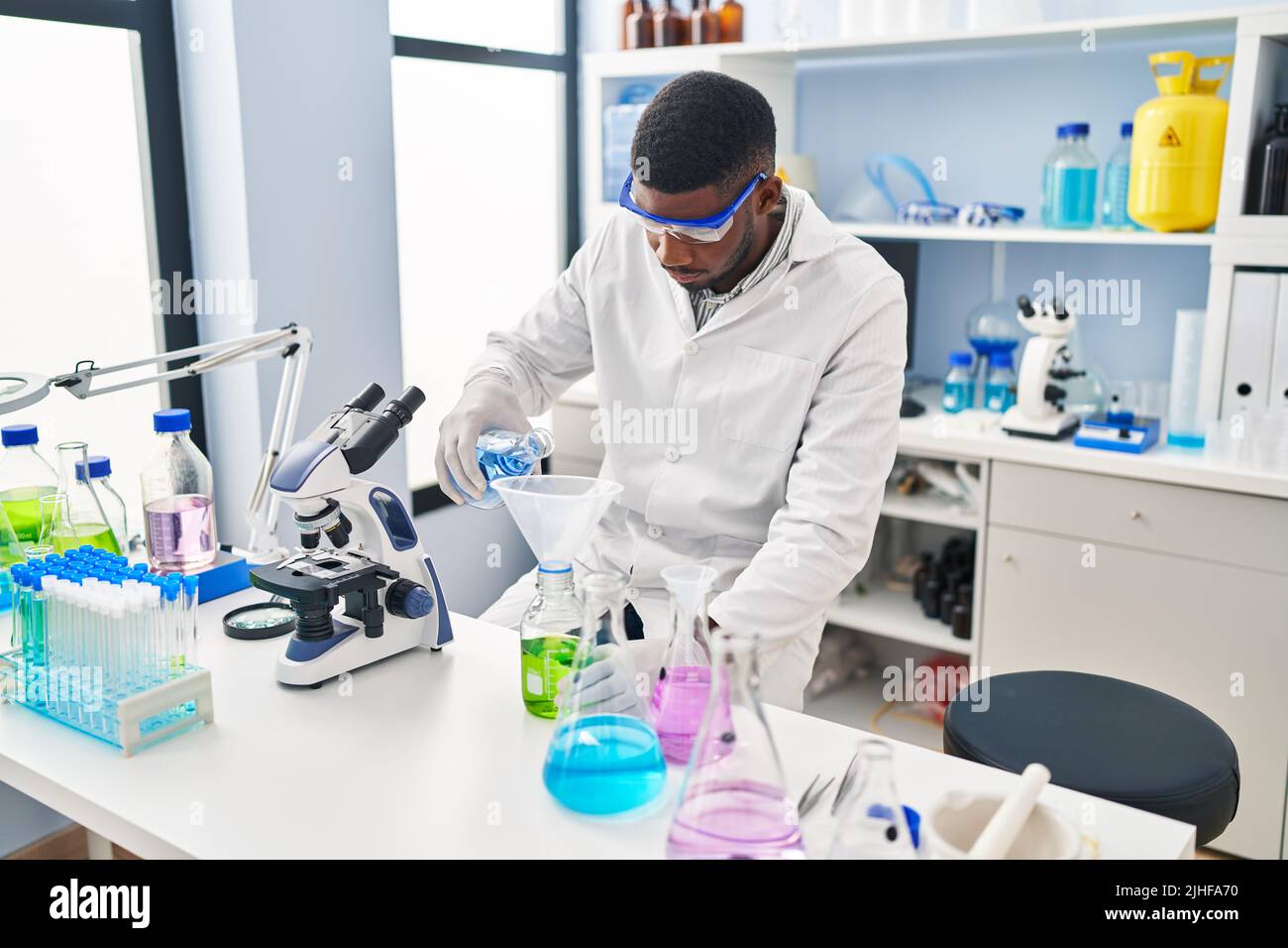Young african american man wearing scientist uniform measuring liquid ...