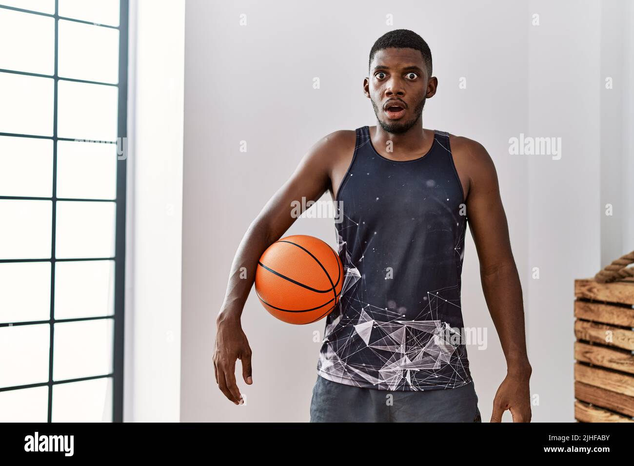 Young african american man holding basketball ball at home scared and ...