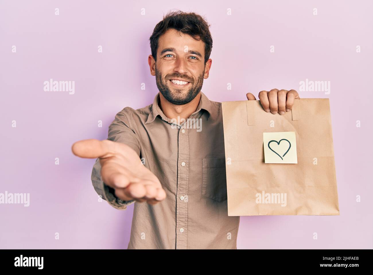 Handsome man with beard holding delivery paper bag with heart reminder ...