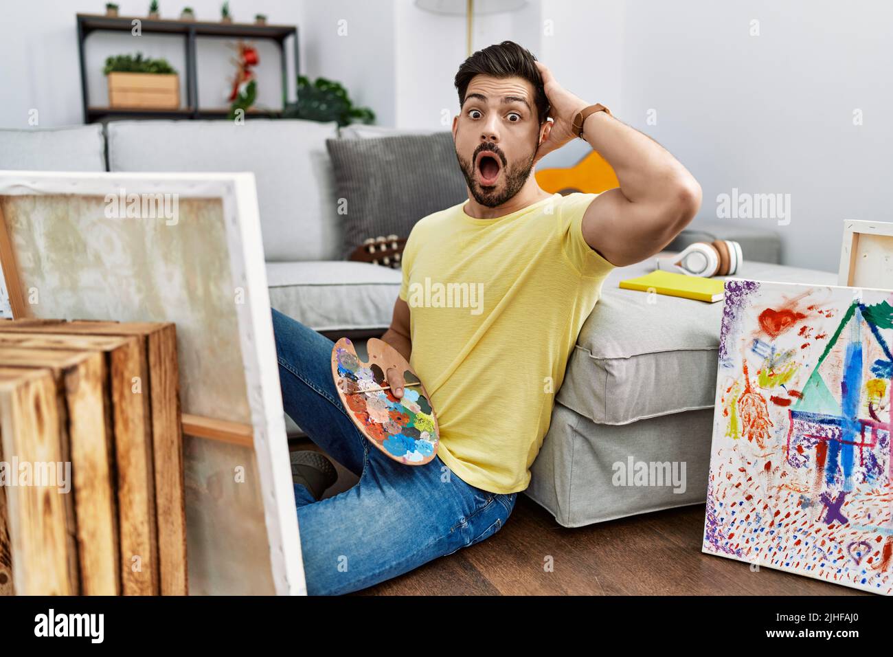 Young man with beard painting canvas at home crazy and scared with ...