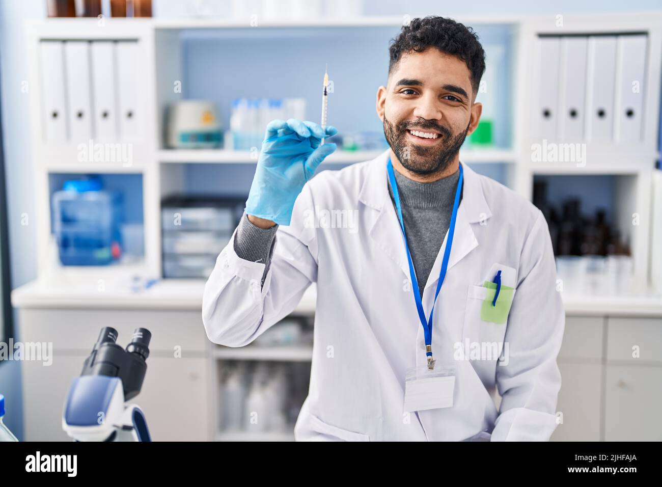 Hispanic man with beard working at scientist laboratory holding syringe ...