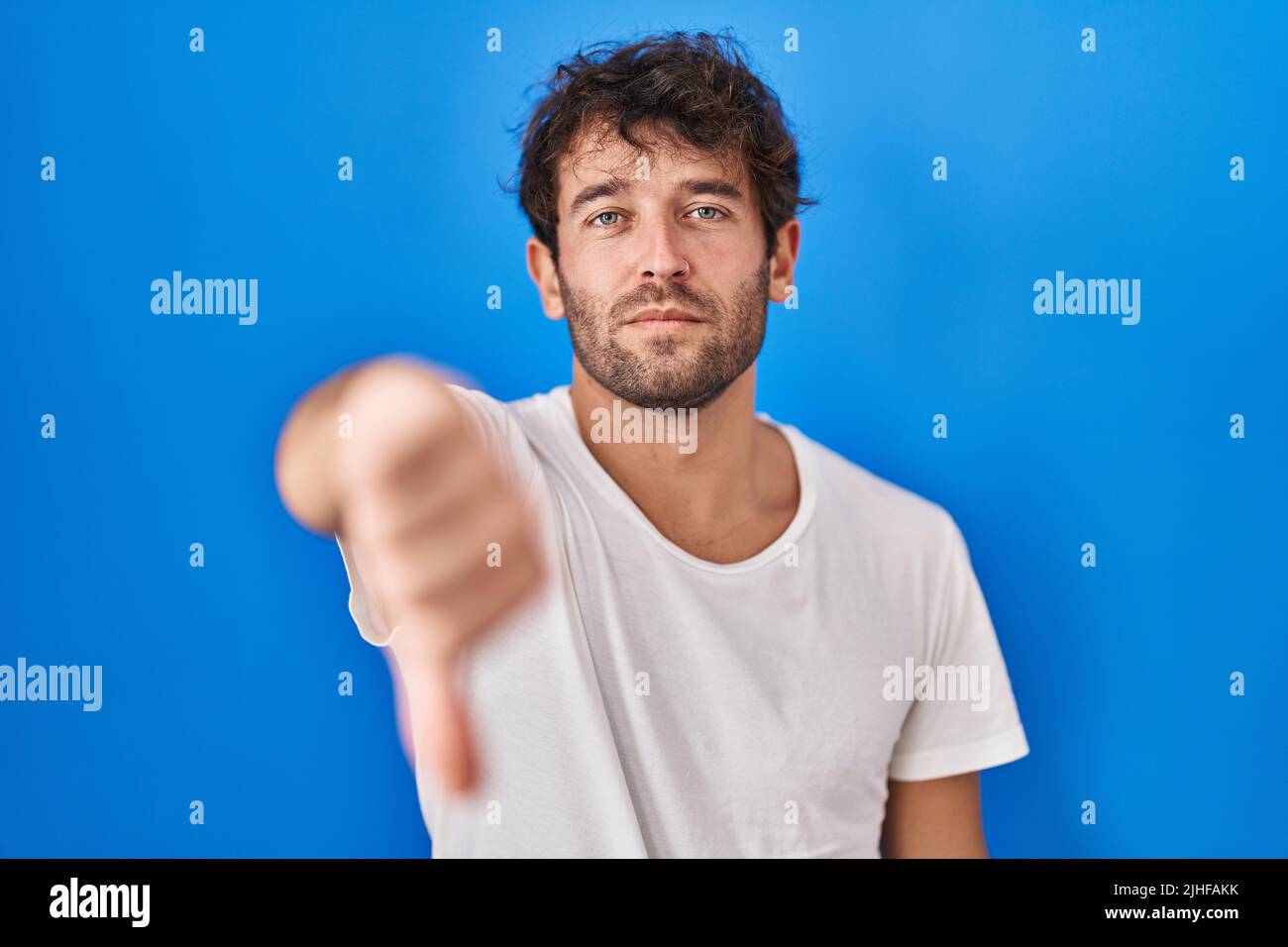 Hispanic young man standing over blue background looking unhappy and ...
