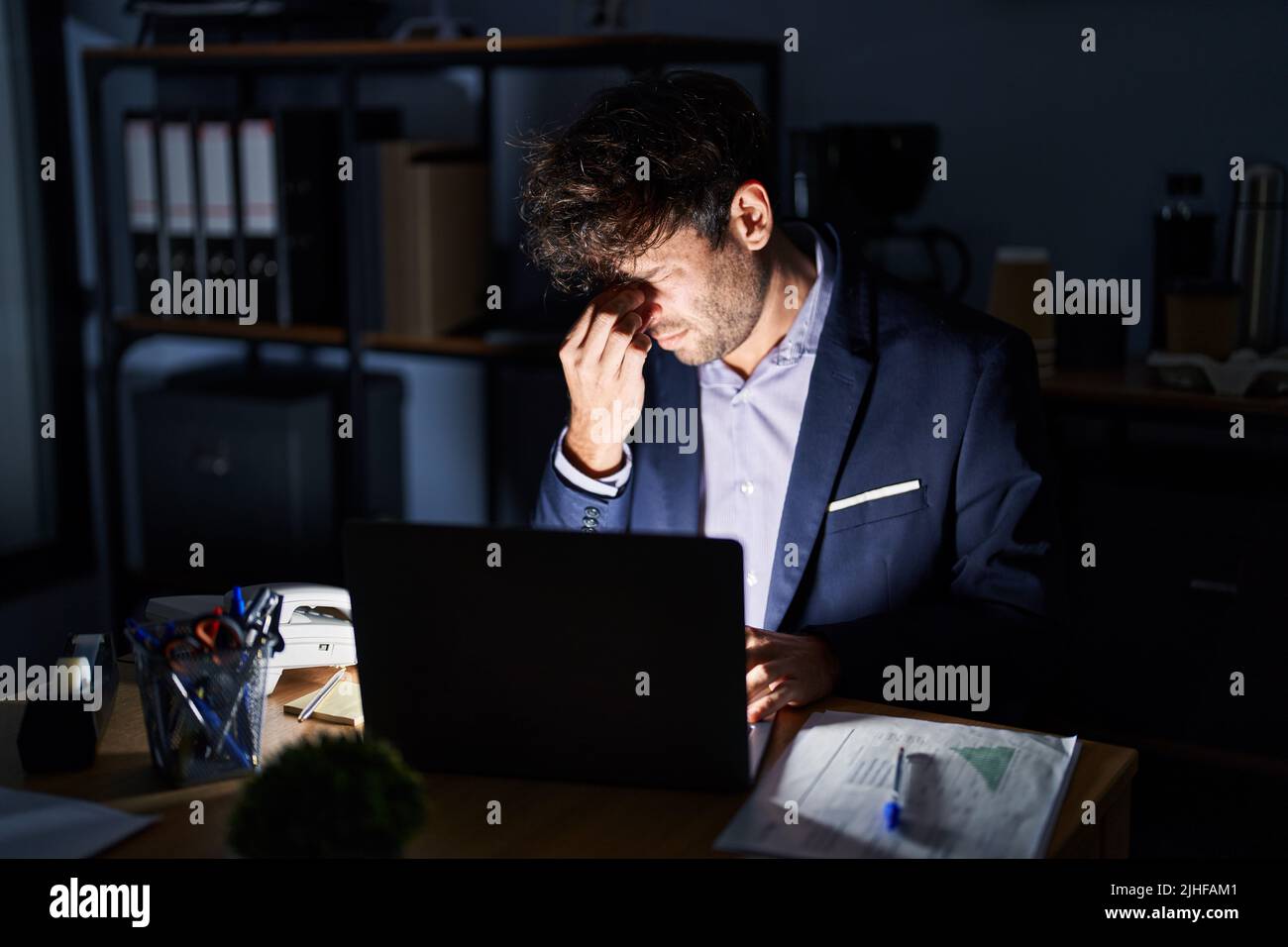 Hispanic young man working at the office at night tired rubbing nose ...