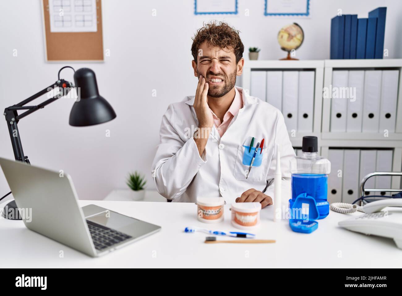 Young hispanic dentist man working at medical clinic touching mouth ...