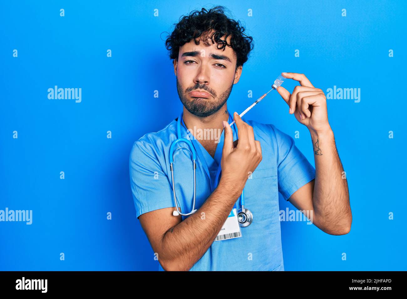 Young hispanic man wearing nurse uniform holding vaccine depressed and ...
