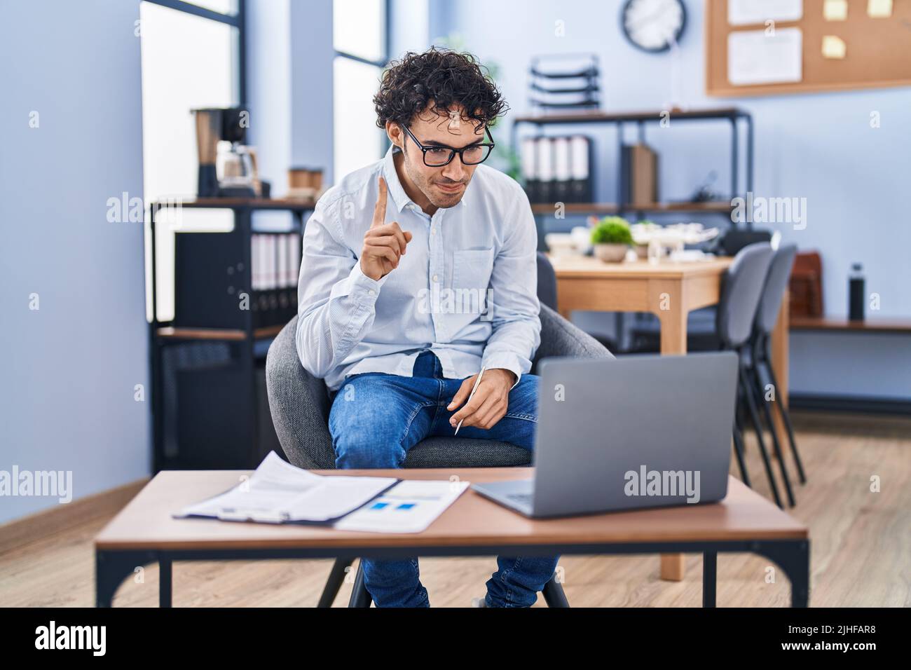 Hispanic man doing video call waving to laptop smiling with an idea or ...