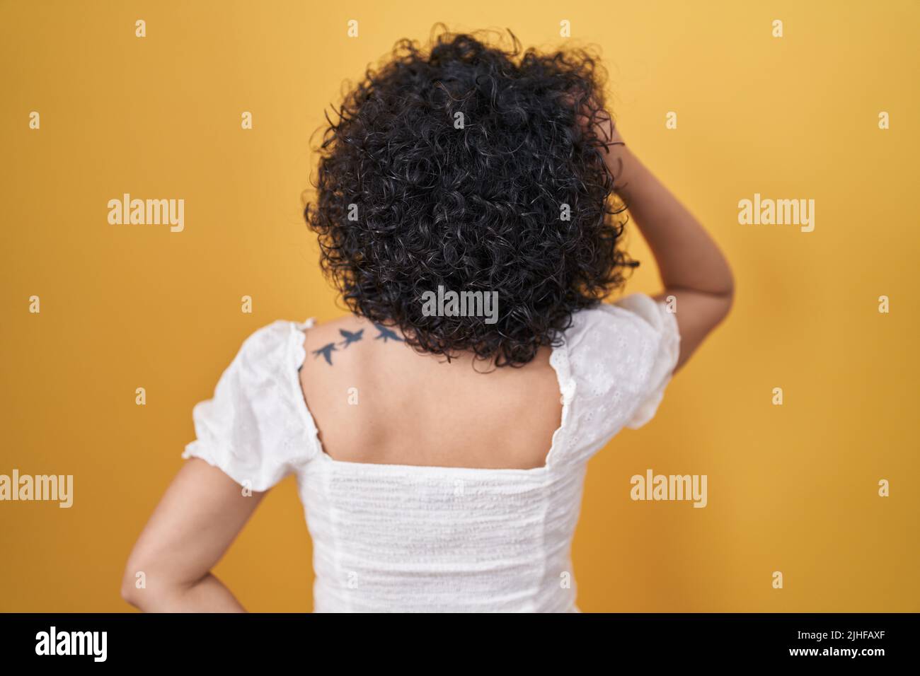 Young brunette woman with curly hair standing over yellow background ...
