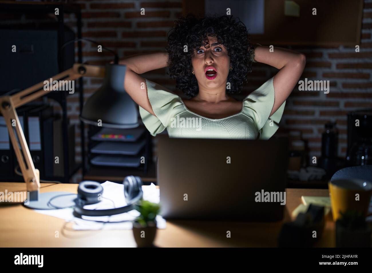 Young brunette woman with curly hair working at the office at night ...