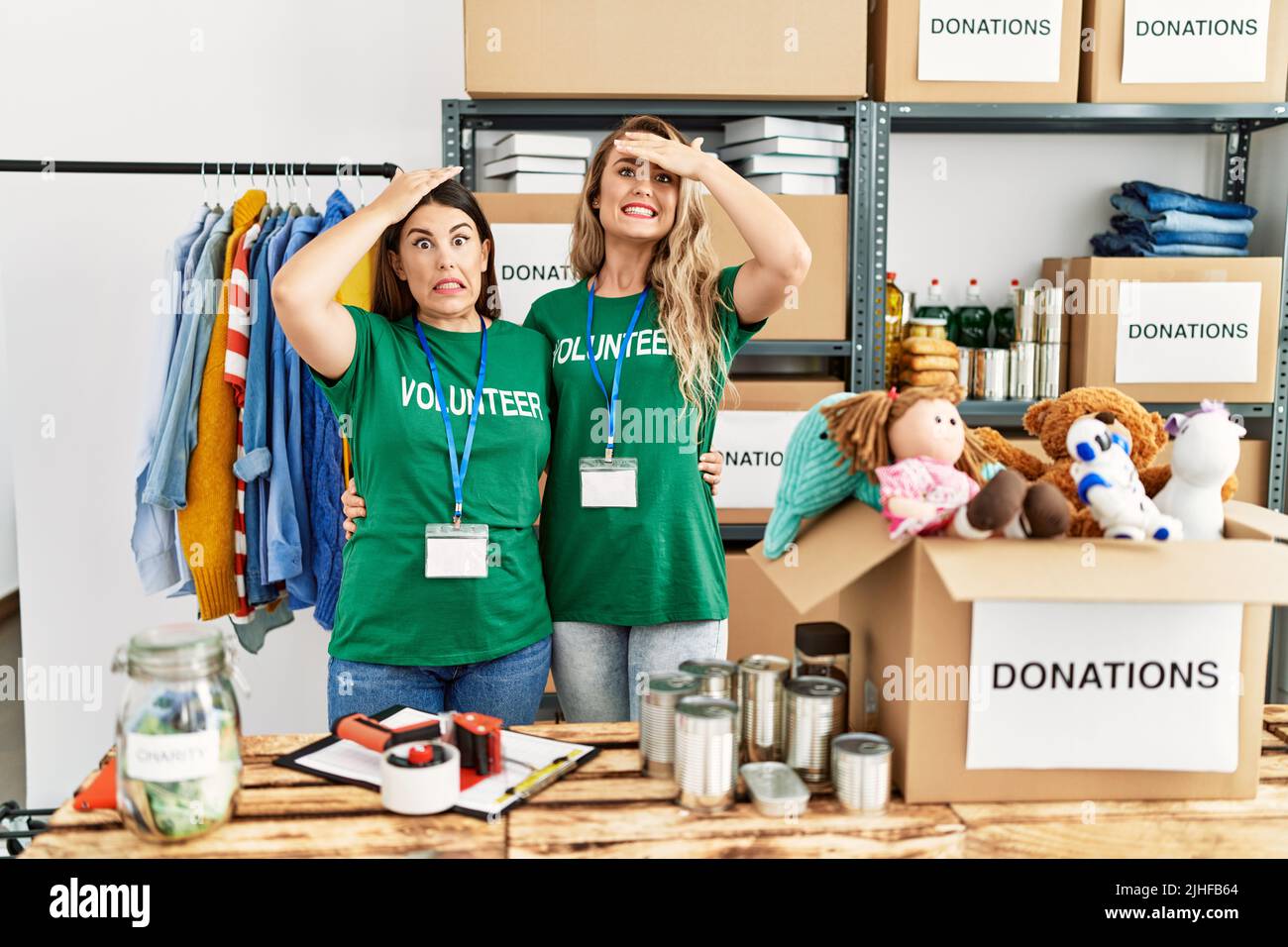 Two young women wearing volunteer t shirt at donations stand stressed and frustrated with hand ...