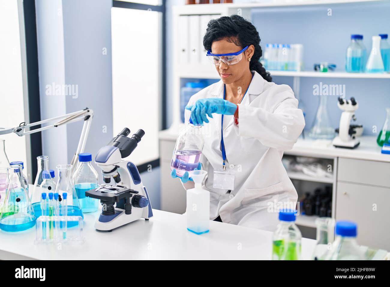 African american woman wearing scientist uniform measuring liquid at ...