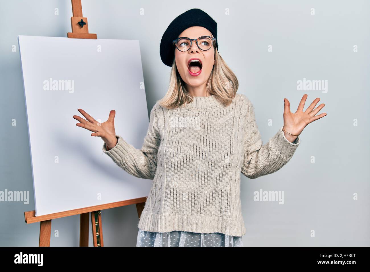 Beautiful caucasian woman standing by painter easel stand crazy and mad ...