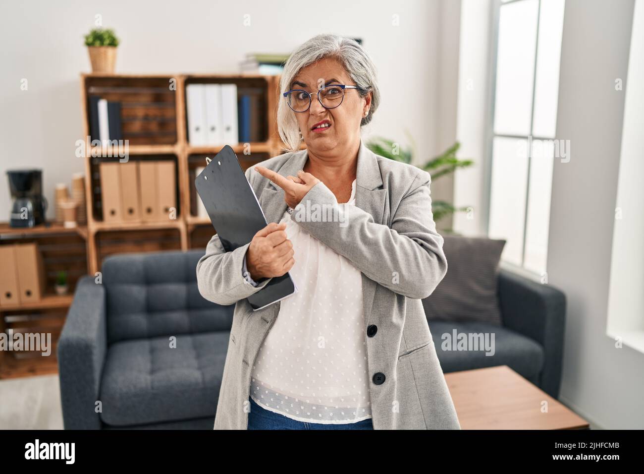 Middle age woman with grey hair at consultation office pointing aside ...