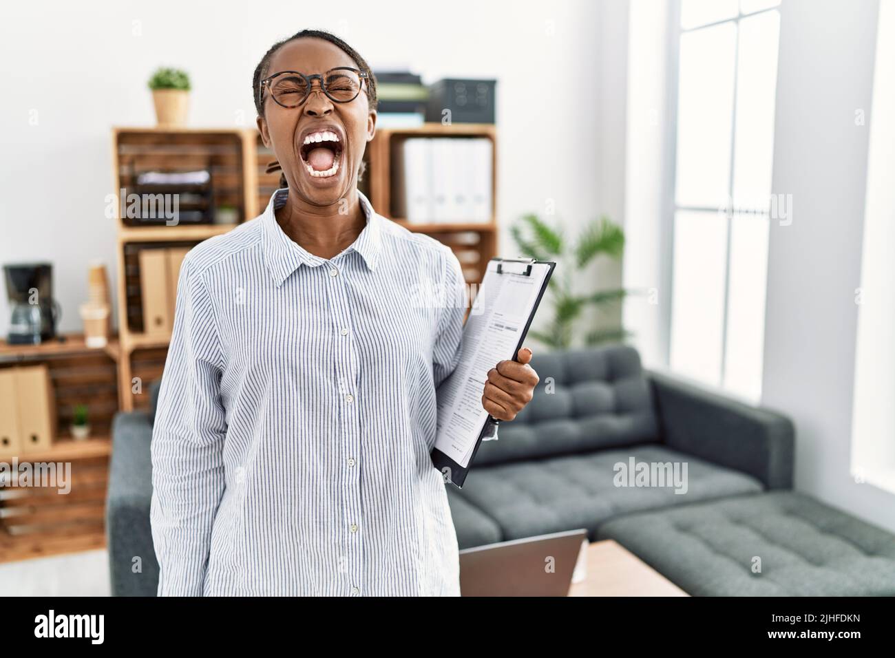 African woman working at psychology clinic angry and mad screaming ...