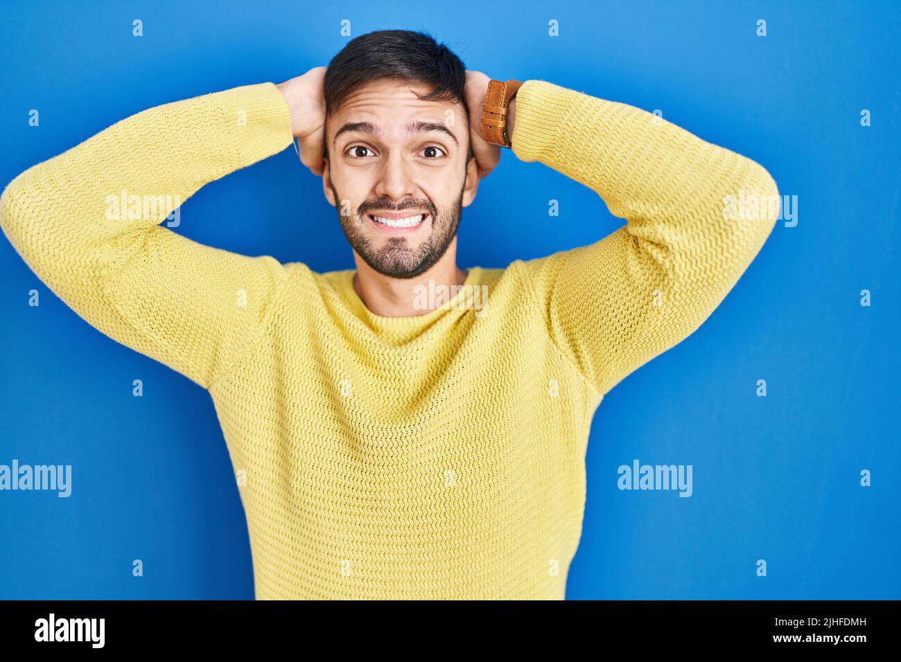 Hispanic man standing over blue background crazy and scared with hands ...