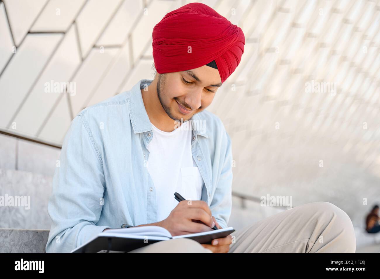 Focused Indian student in traditional turban sitting outdoors with ...