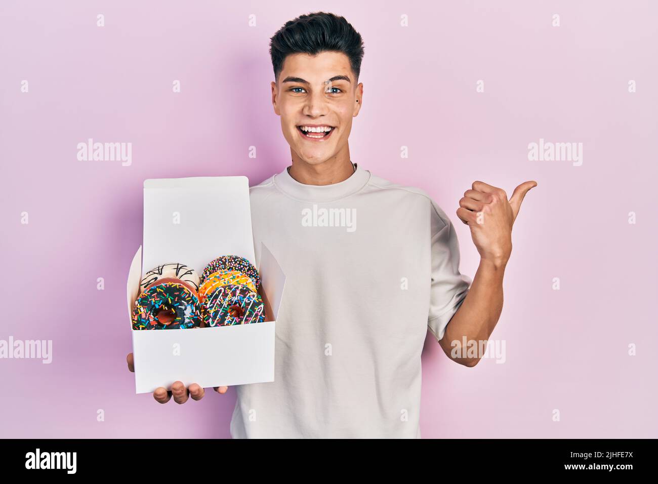 Young hispanic man holding box of tasty colorful doughnuts pointing ...