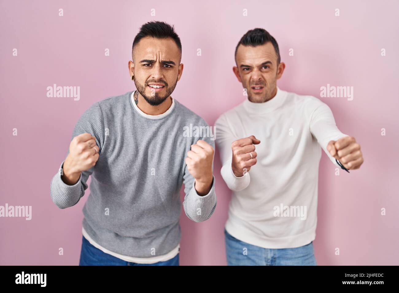 Homosexual couple standing over pink background angry and mad raising ...