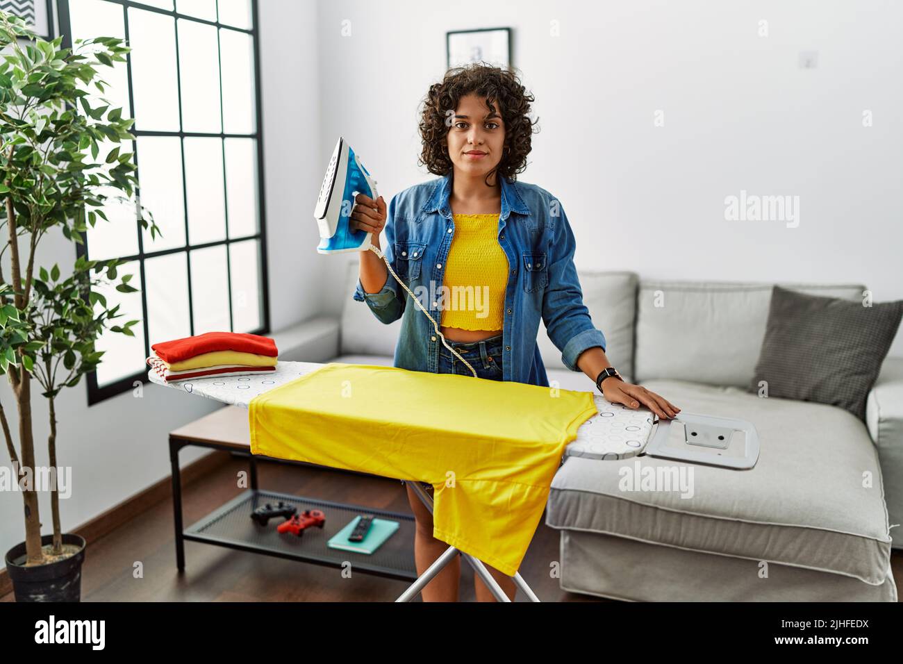 Young hispanic woman ironing clothes at home relaxed with serious ...