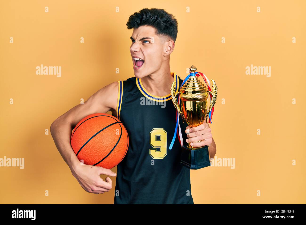 Young hispanic man wearing basketball uniform holding ball and prize ...