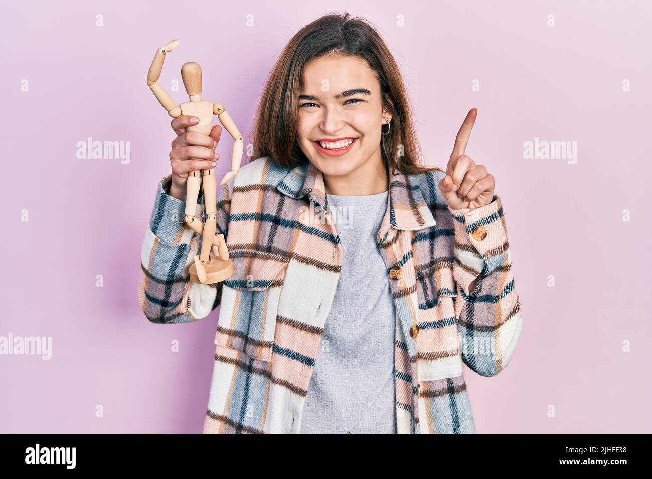 Young caucasian girl holding small wooden manikin smiling with an idea ...