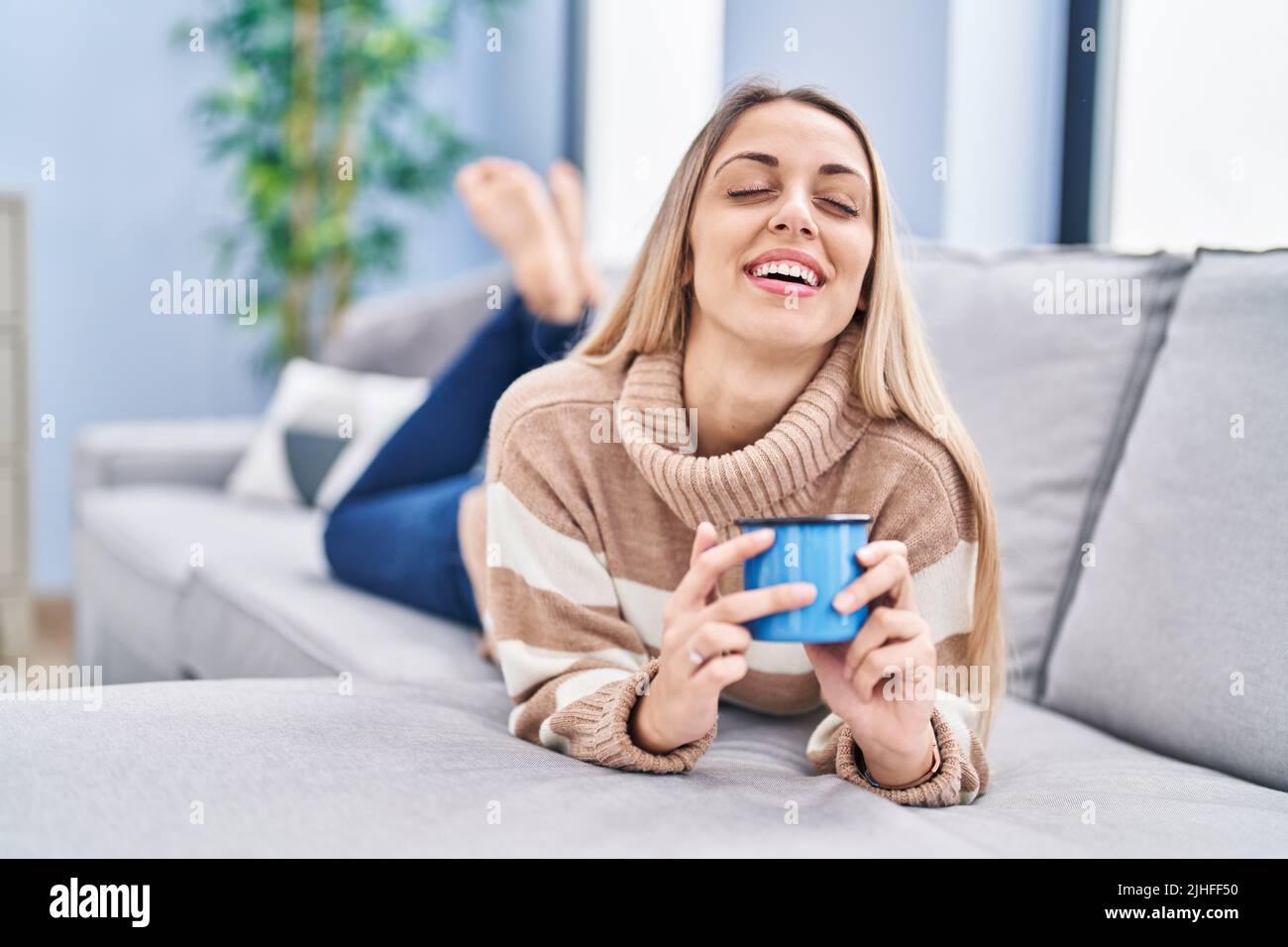 Young woman drinking coffee lying on sofa at home Stock Photo - Alamy