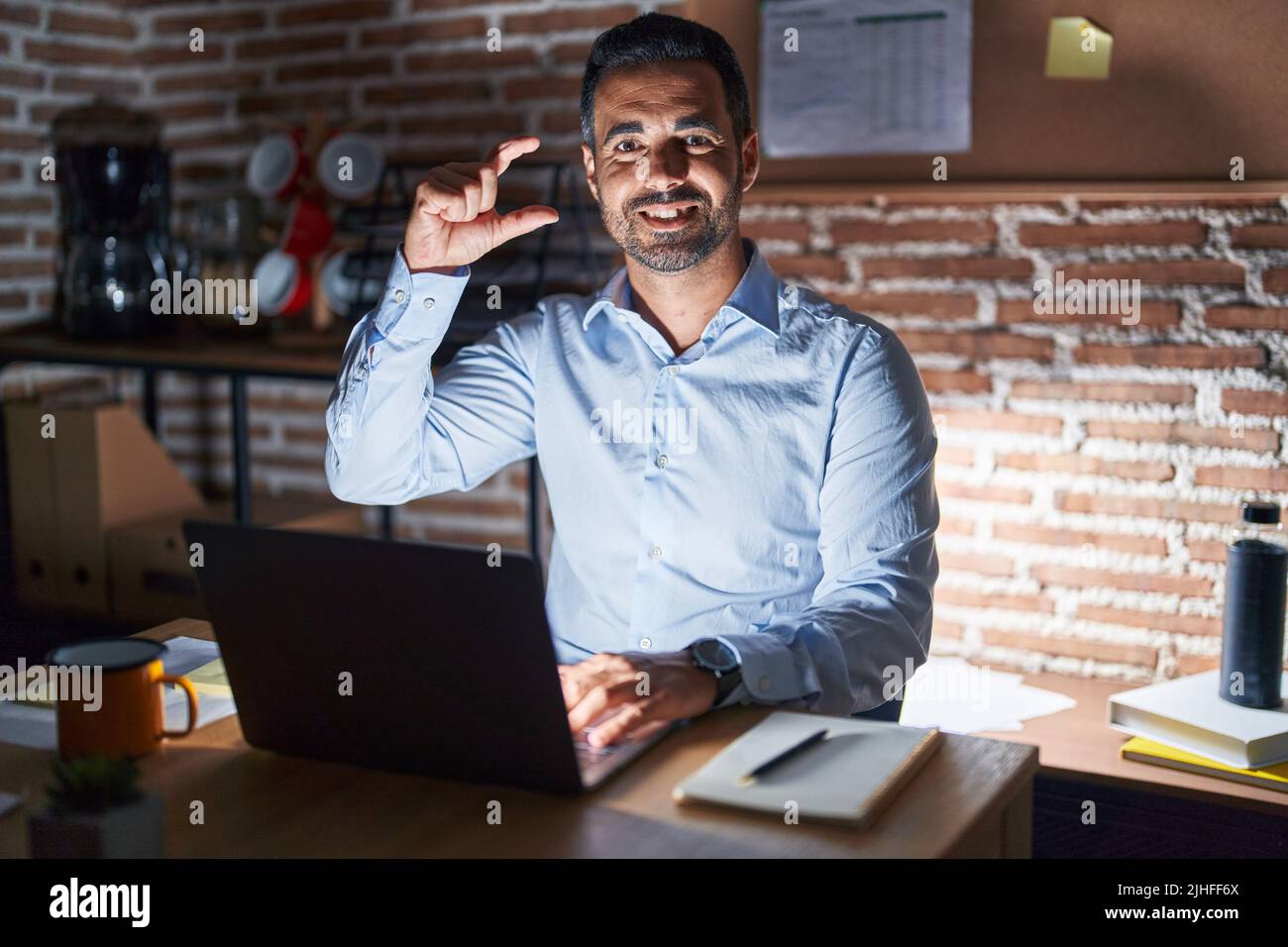 Hispanic man with beard working at the office at night smiling and ...