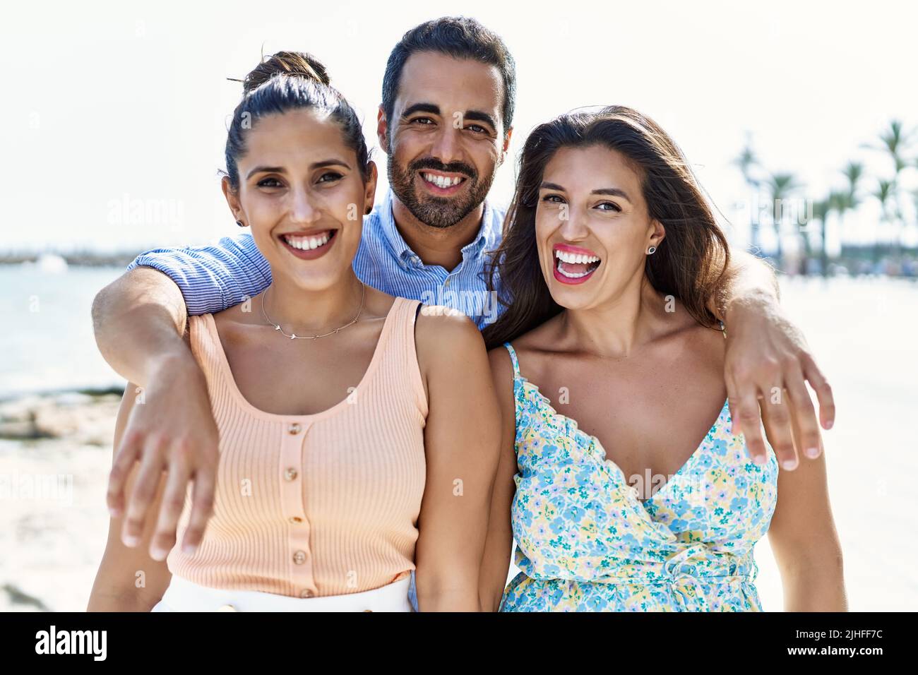 Three young hispanic friends smiling happy and hugging at the beach ...