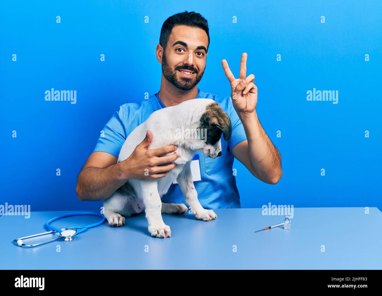 Handsome hispanic veterinary man with beard checking dog health smiling ...