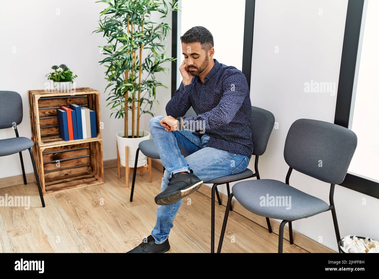 Young hispanic man desperate sitting on chair at waiting room Stock ...