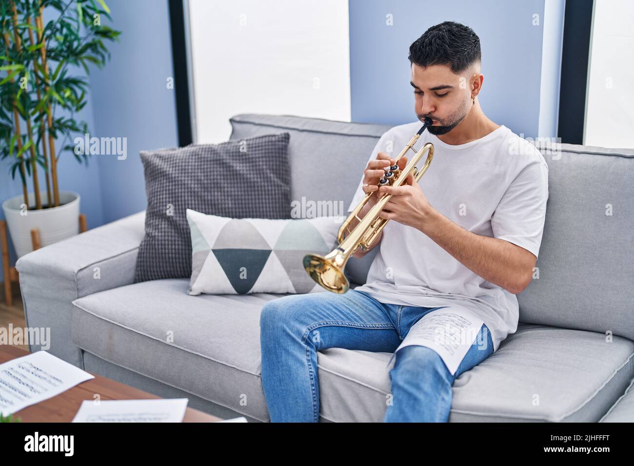 Young arab man musician playing trumpet sitting on sofa at home Stock ...