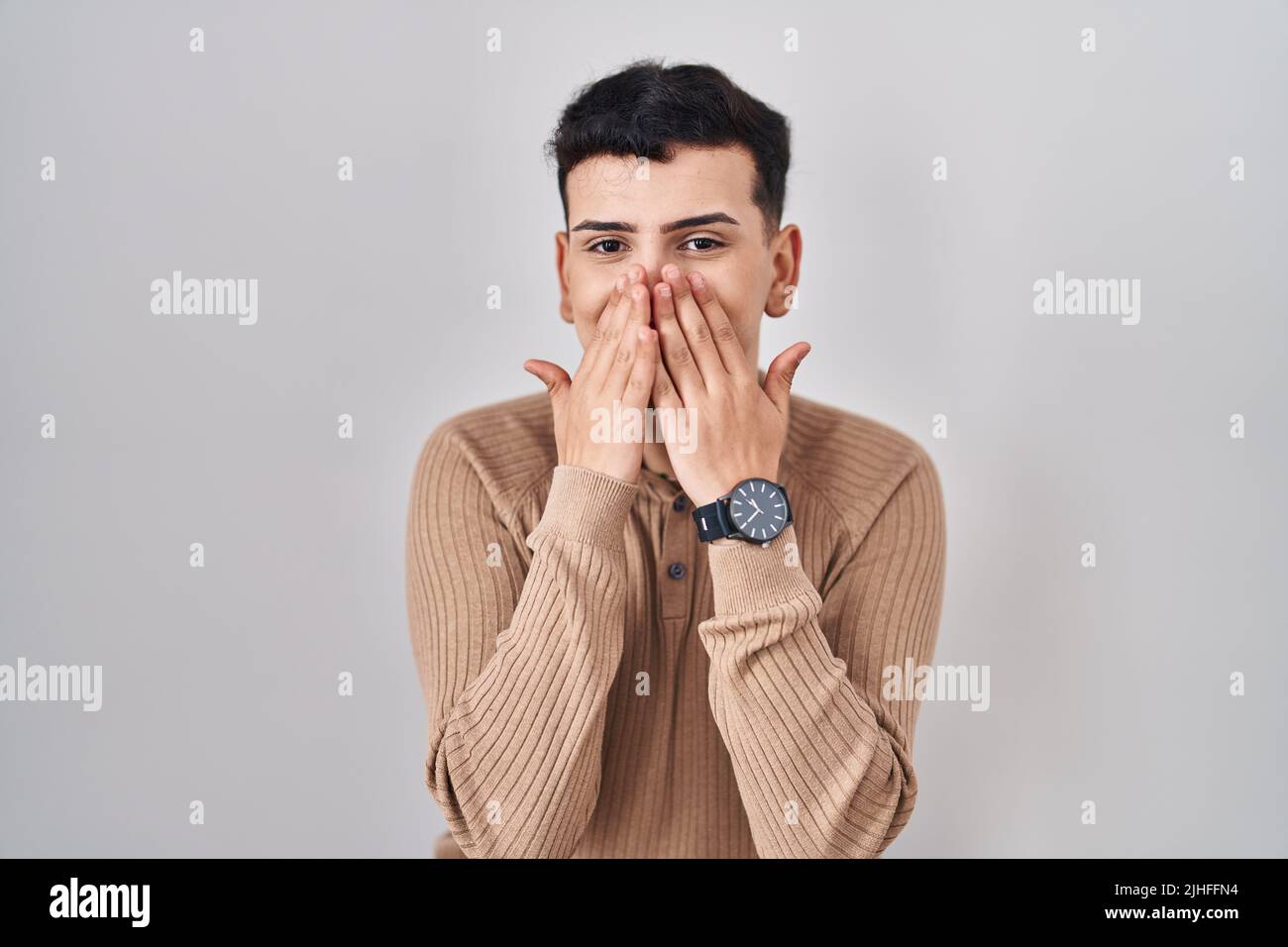 Non binary person standing over isolated background laughing and embarrassed giggle covering ...