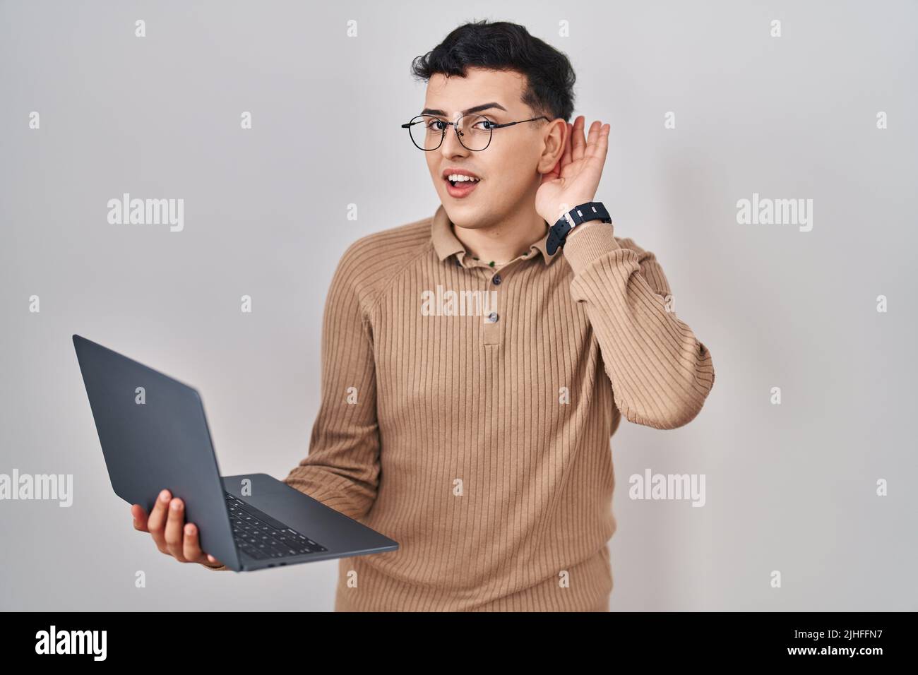 Non binary person using computer laptop smiling with hand over ear ...