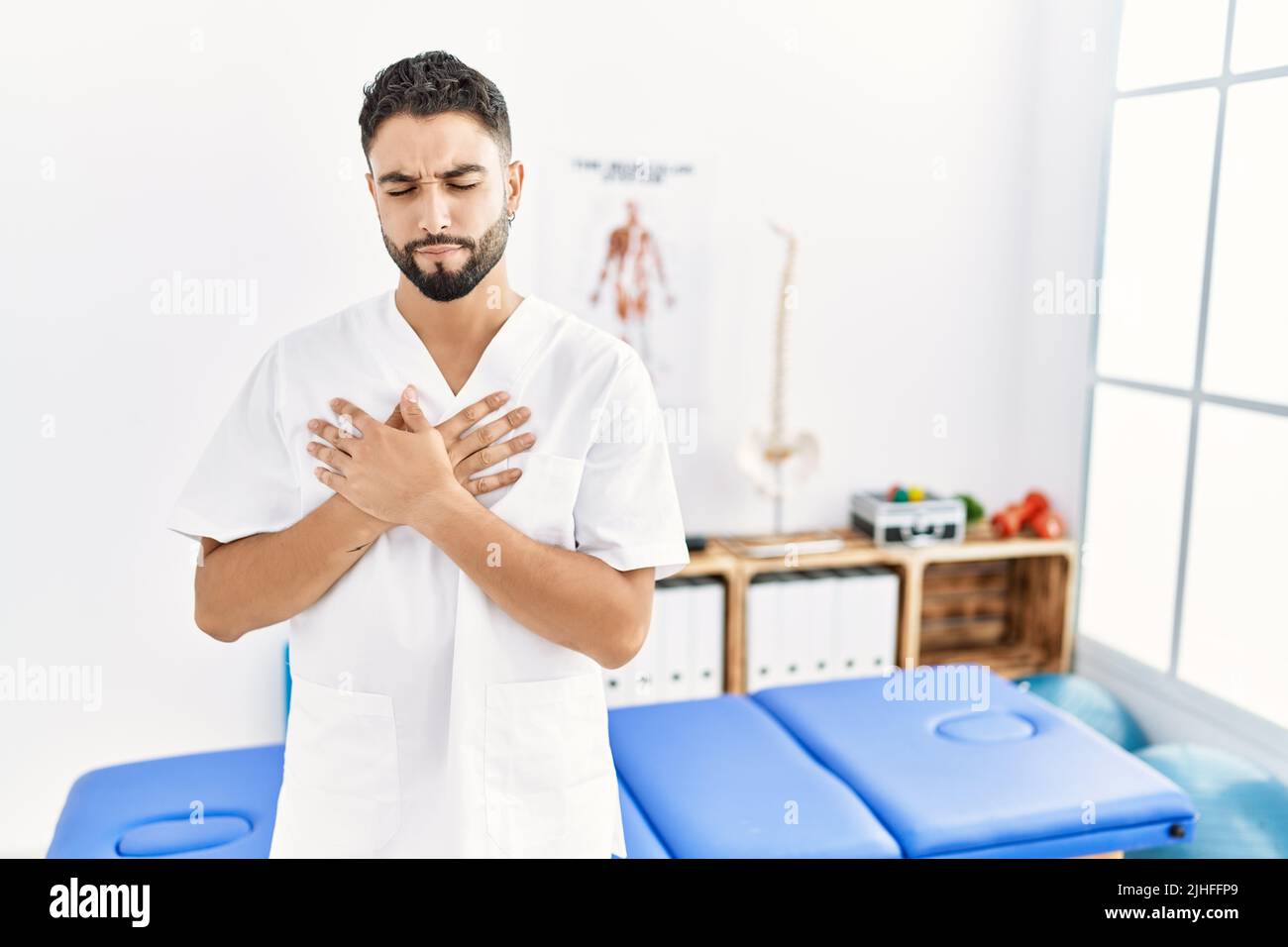 Young handsome man with beard working at pain recovery clinic smiling ...