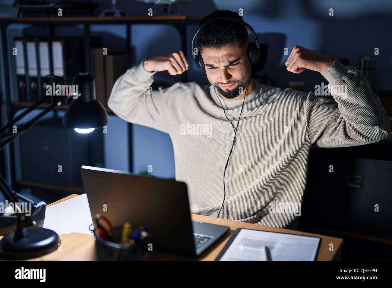 Young handsome man working using computer laptop at night showing arms ...