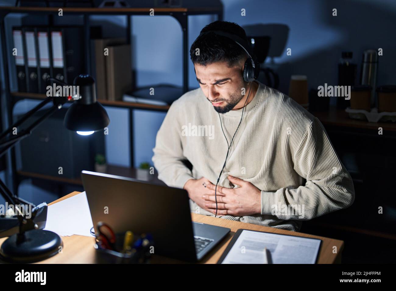 Young handsome man working using computer laptop at night with hand on ...