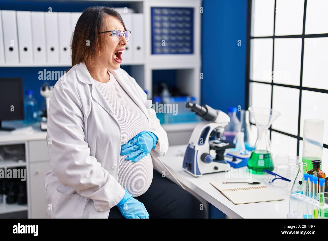 Pregnant woman working at scientist laboratory angry and mad screaming ...