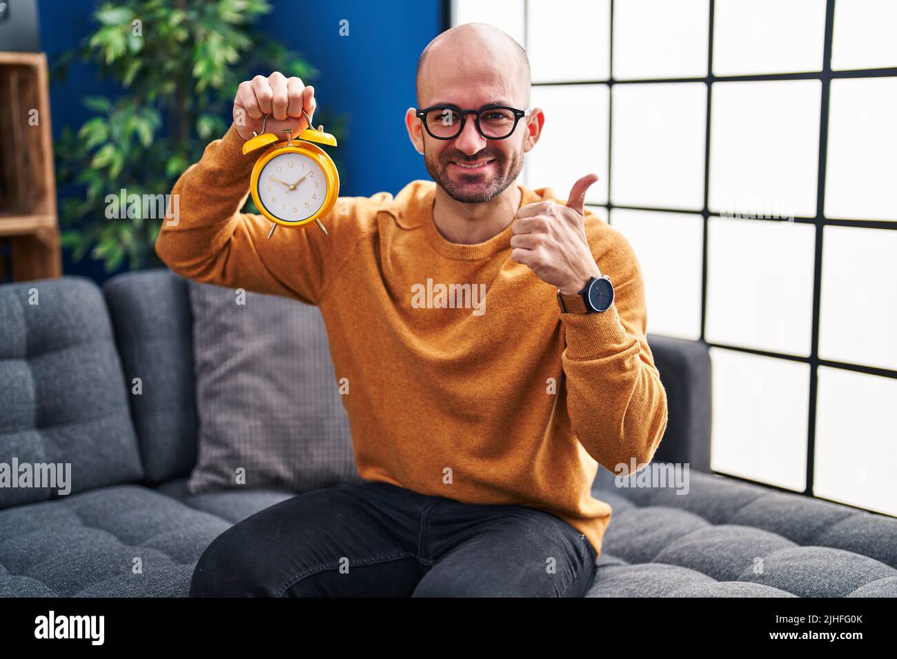 Young bald man with beard holding alarm clock smiling happy and ...